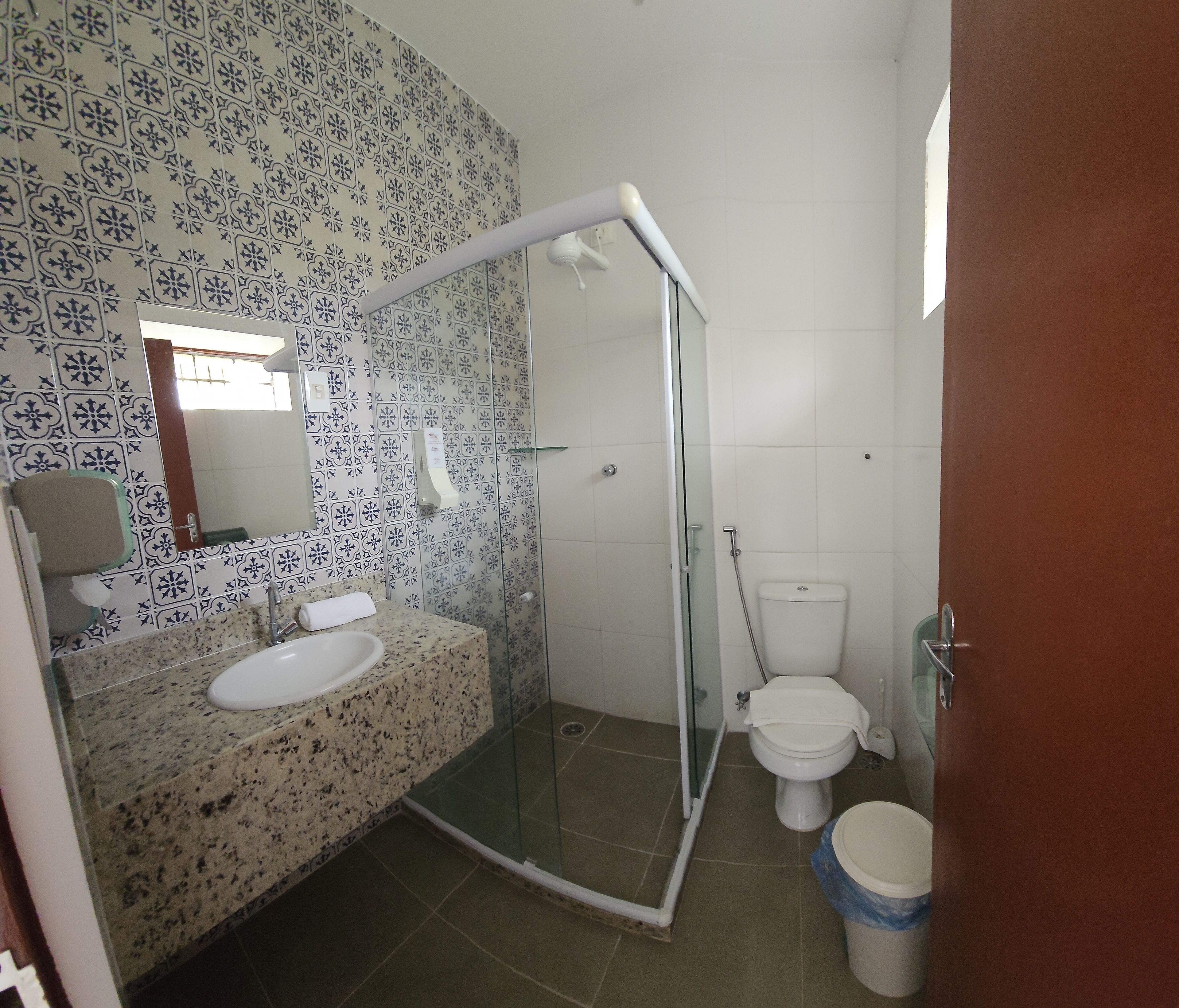Casa de banho com chuveiro de vidro, lavatório com espelho e duas sanitas.