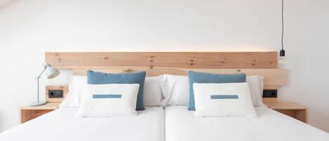 Uma cama de casal bem arrumada com roupa de cama branca e azul, uma cabeceira de madeira e um abajur sobre uma mesa de cabeceira de madeira.