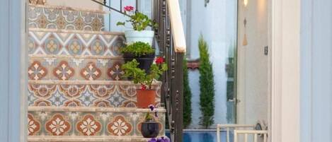 Uma escadaria com ladrilhos estampados, plantas em vasos e um banco em um corredor.