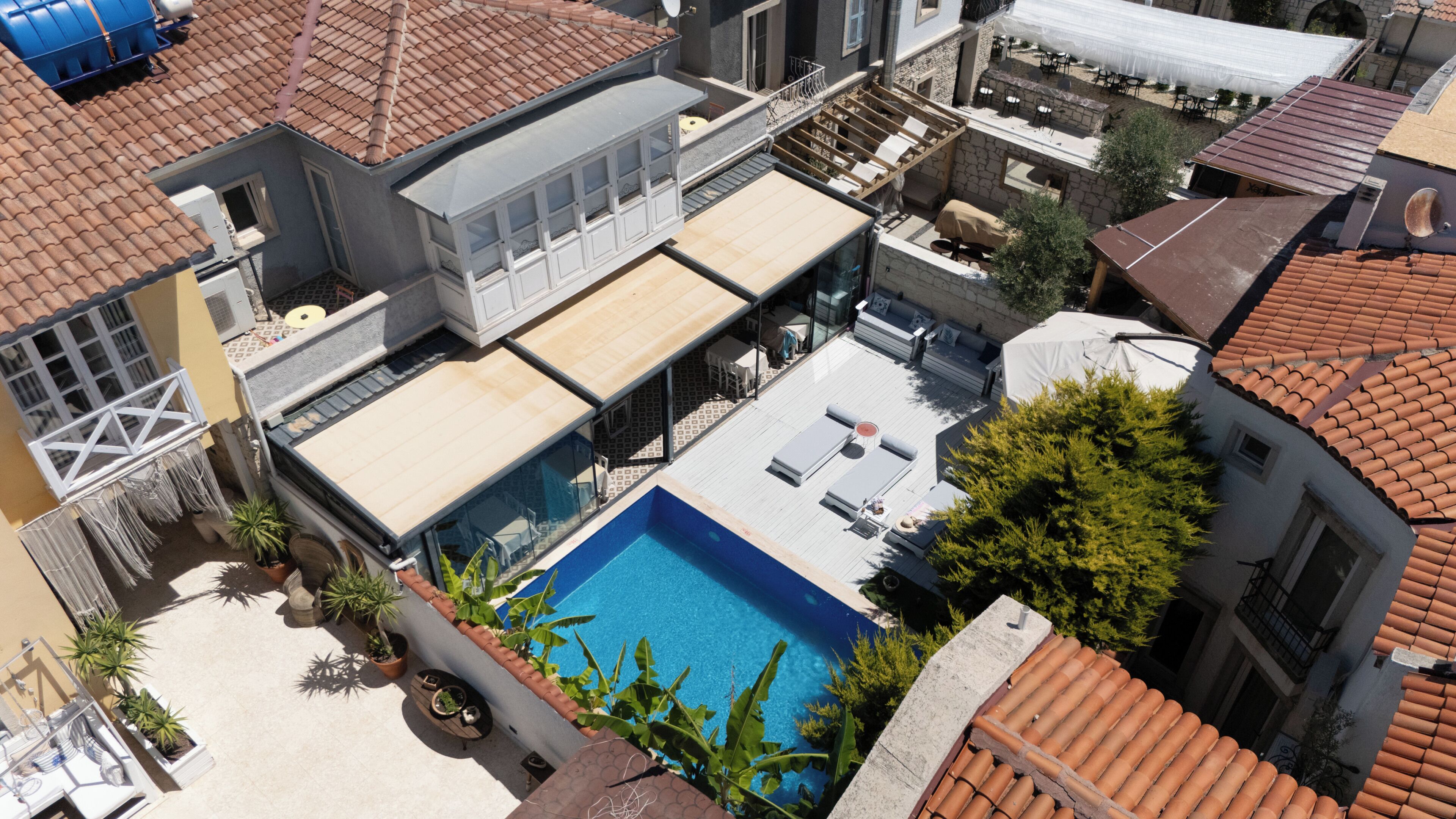 Uma área de piscina no terraço com piscina azul límpida, cercada por mobiliário de exterior e plantas em vasos.