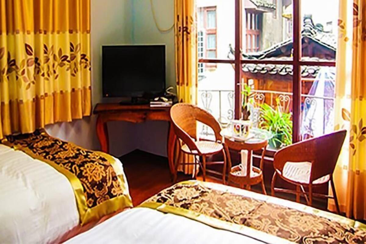 Quarto de hotel com uma cama, uma escrivaninha com televisão, uma cadeira e uma mesa com uma planta.