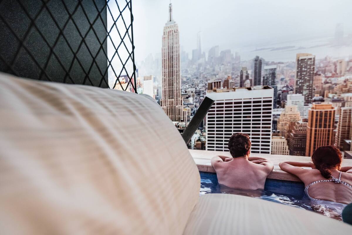 Um casal relaxando em uma piscina infinita no terraço, com vista para o horizonte urbano, incluindo um arranha-céu imponente.