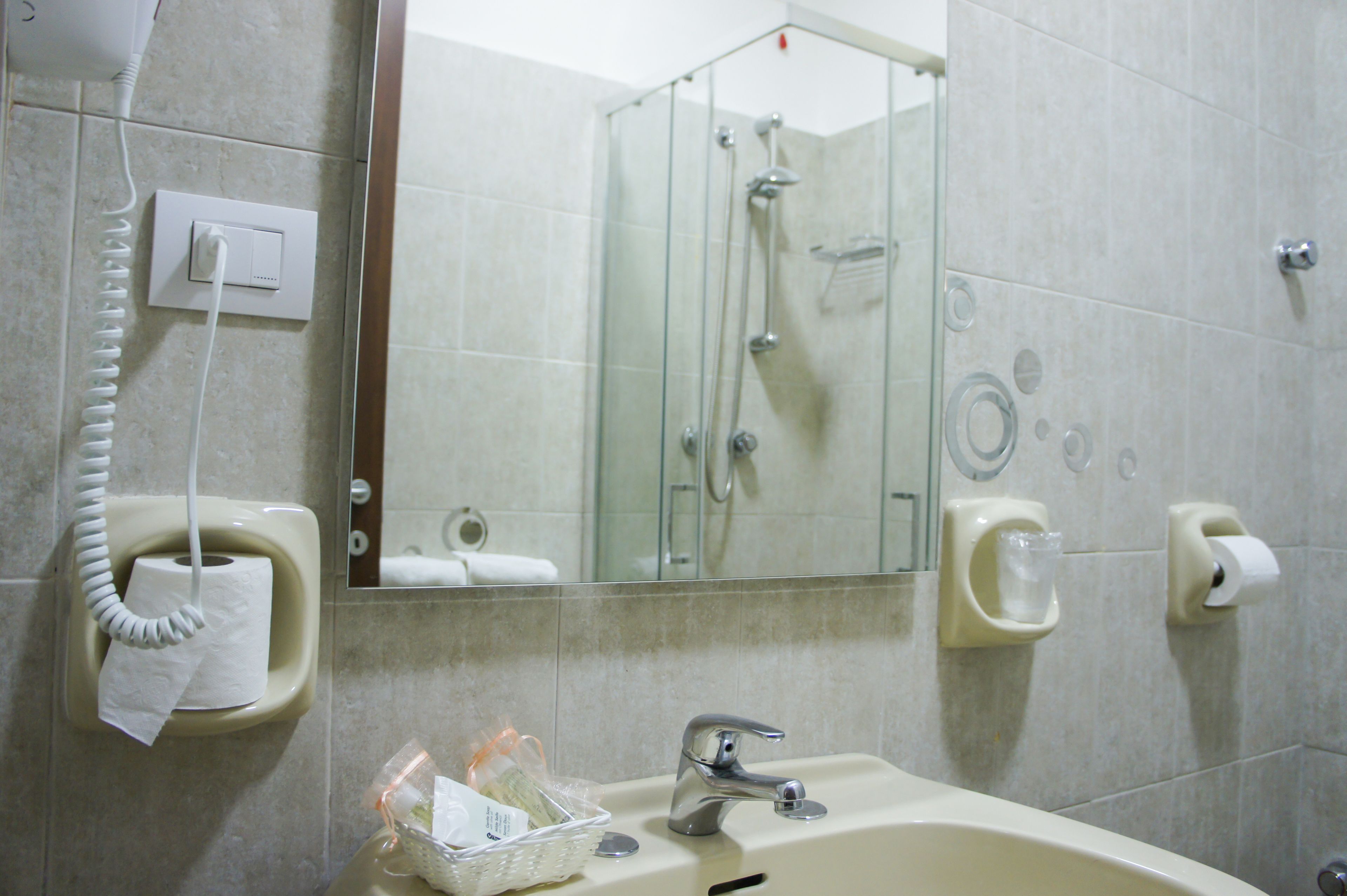 Casa de banho com lavatório, espelho, chuveiro e suporte para papel higiénico.