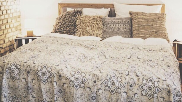 Quarto com colcha estampada, cabeceira de madeira e parede de tijolos.