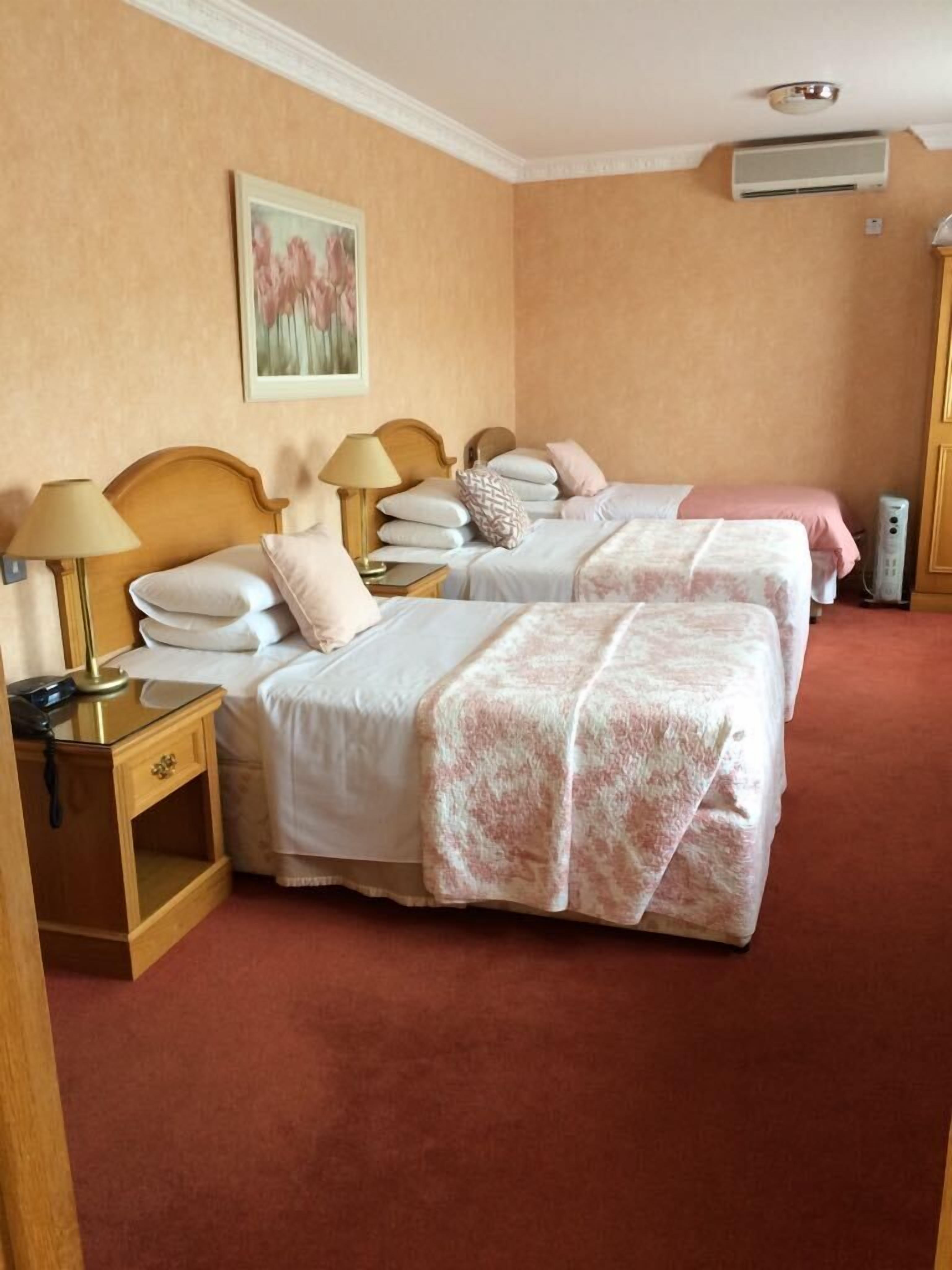 Quarto de hotel com duas camas, uma mesa de cabeceira com abajur, um quadro na parede e um aparelho de ar condicionado.