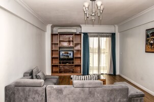 Uma sala de estar com um sofá cinzento, um rack de madeira e um candelabro.