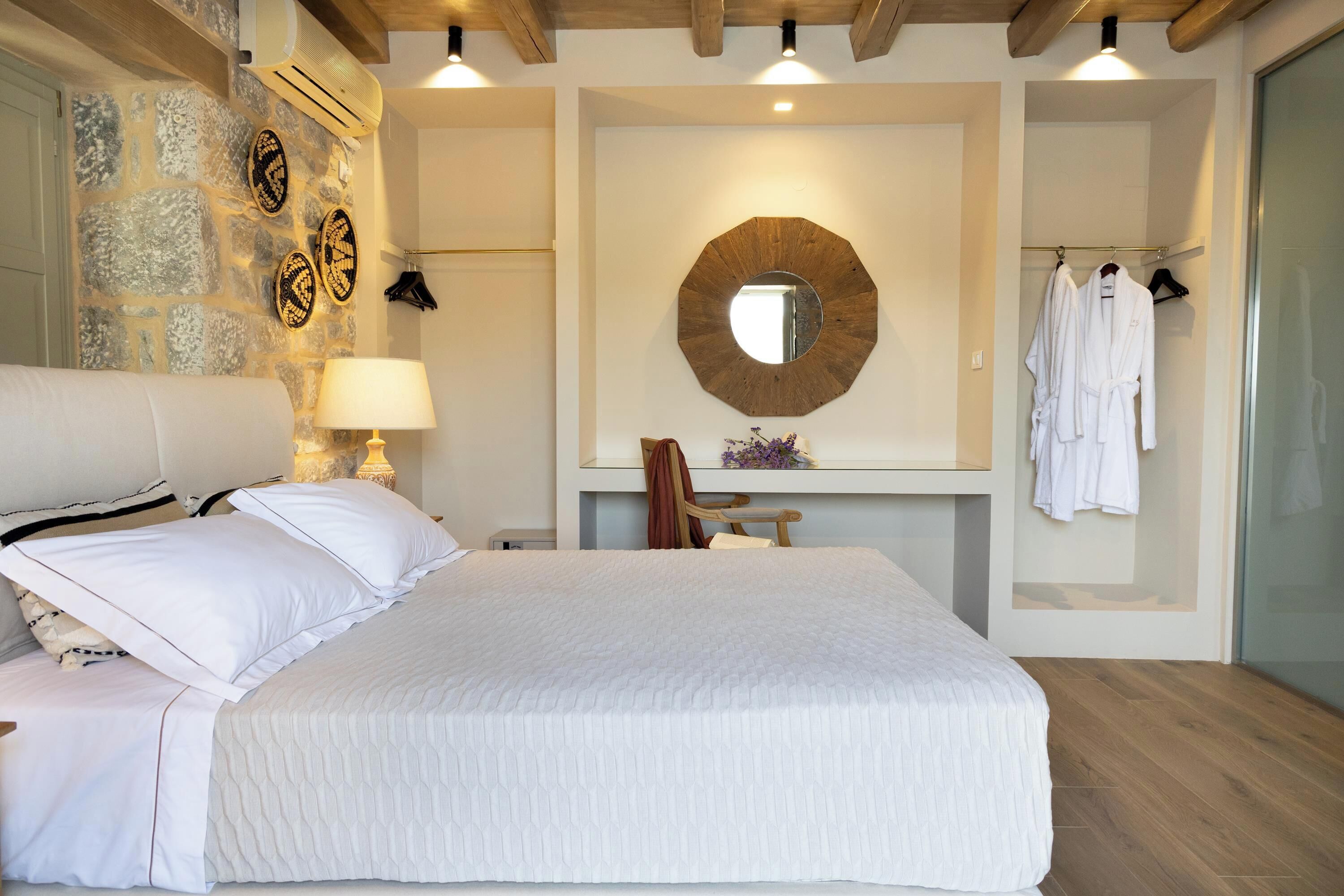 Quarto com cama grande, parede de pedra, espelho, penteadeira e porta-robes.