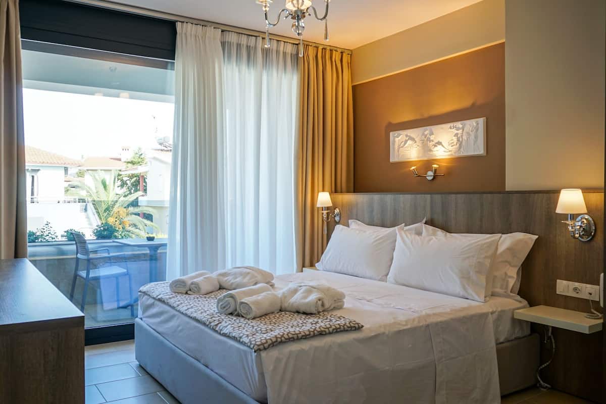 Quarto de hotel com cama, abajures, vista para o exterior e uma pequena mesa com cadeiras.