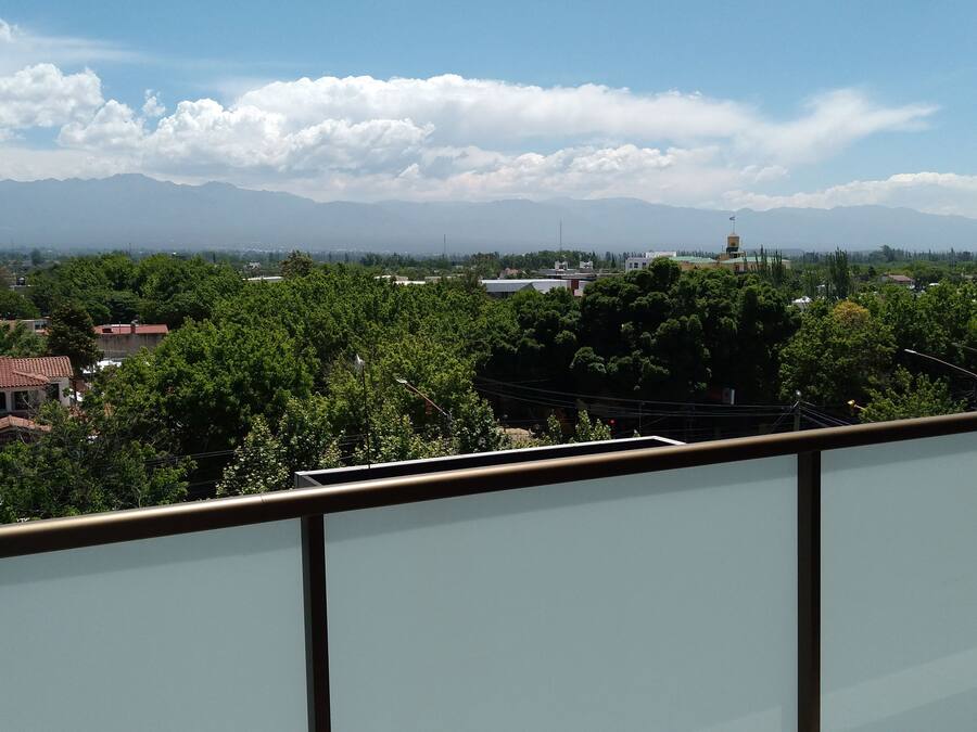 Vista de varanda sobre uma paisagem urbana com edifícios, árvores e montanhas ao longe.