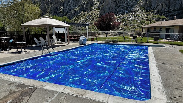 Uma piscina com capa azul, rodeada por espreguiçadeiras e uma área com sombra.