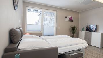 Quarto moderno com cama, mesa de cabeceira, abajur e uma televisão em um penteadeiro.