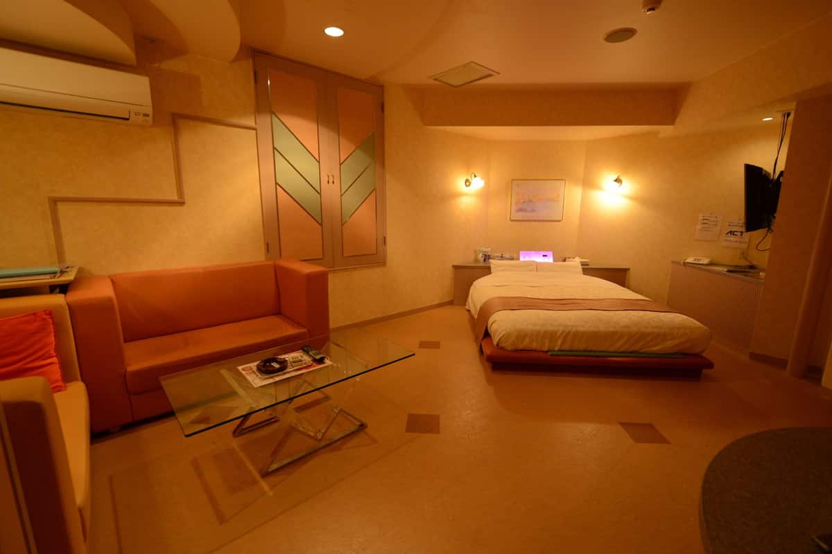 Quarto de hotel com uma cama, uma mesa de centro de vidro, um sofá e uma televisão.