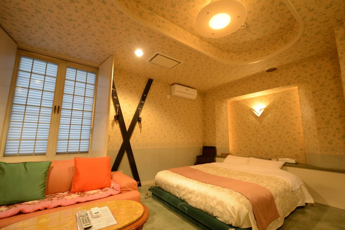 Quarto de hotel com cama, sofá, mesa pequena e janela com persianas.