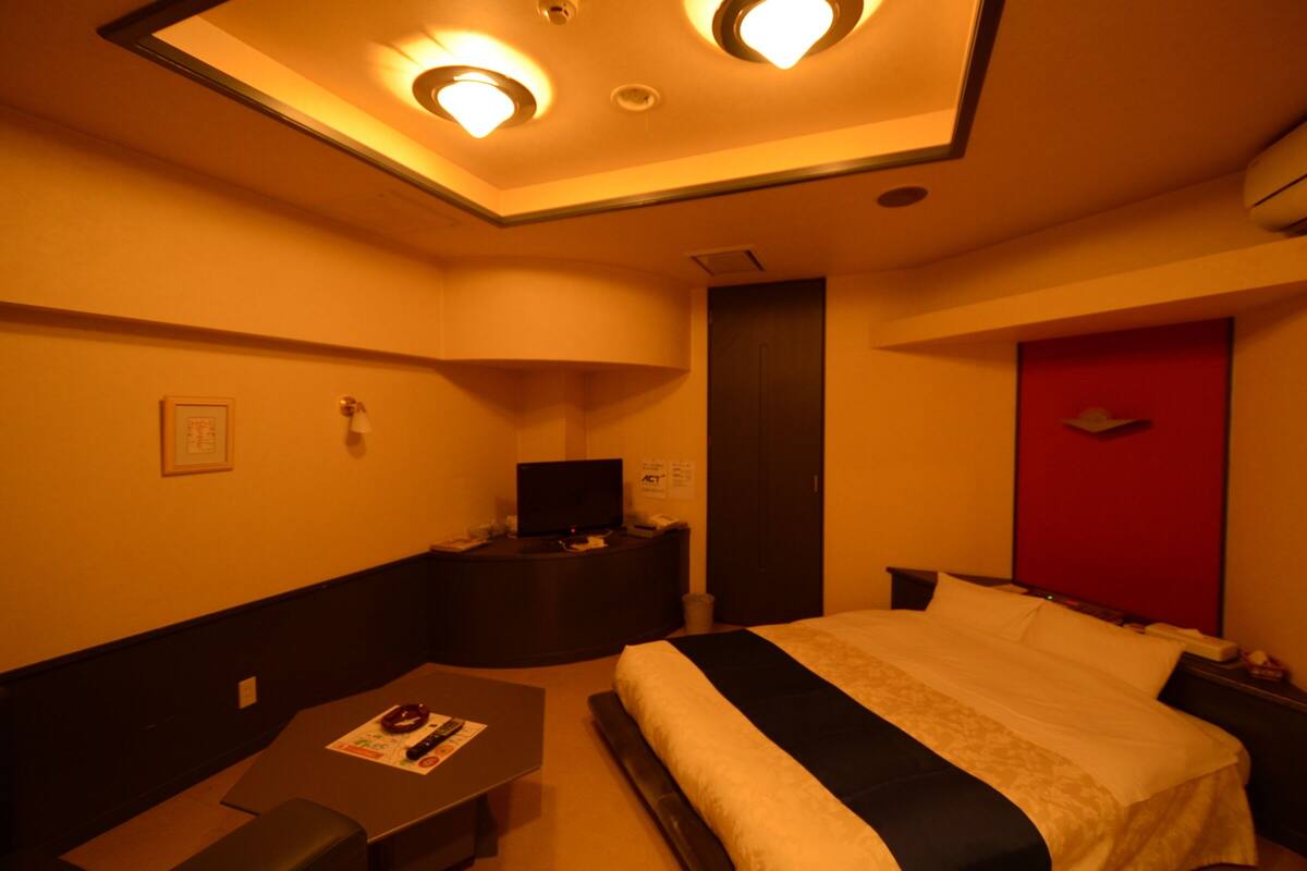Quarto de hotel com cama, escrivaninha e televisão.