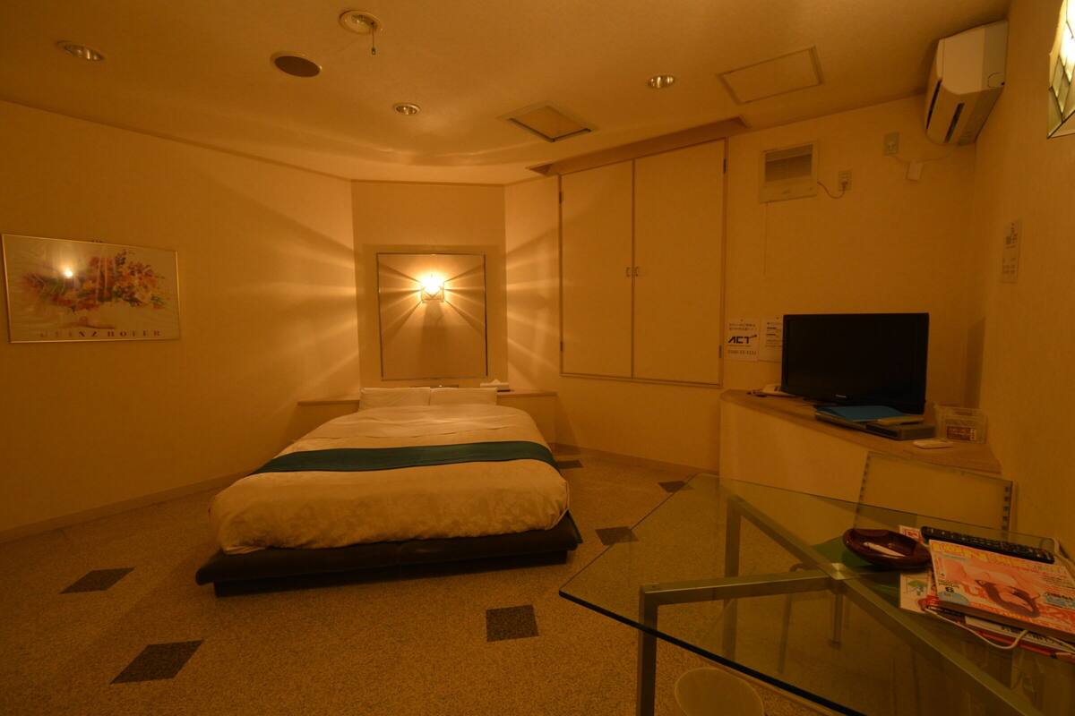 Quarto de hotel com cama, mesa de vidro com controle remoto, televisão e ar condicionado na parede.