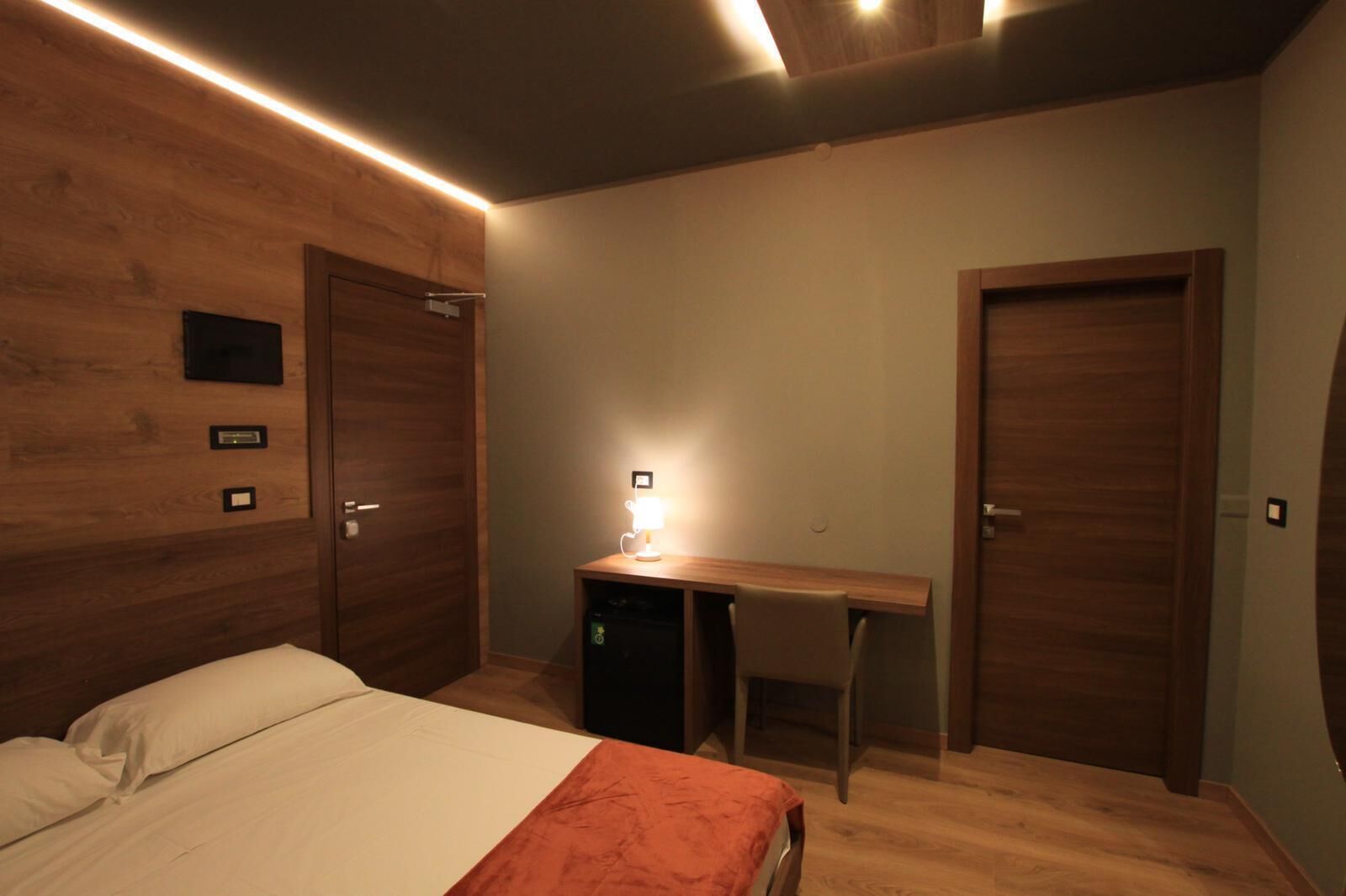 Quarto com cama, escrivaninha e duas portas.