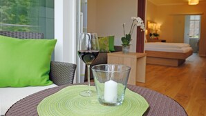 Quarto com cama, um copo de vinho tinto, uma vela e vista para o verde lá fora.