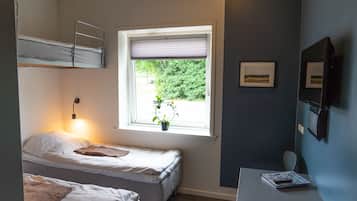Quarto com duas camas, janela com vista para áreas verdes, escrivaninha com cadeira e televisão na parede.