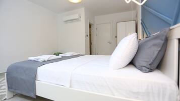 Quarto moderno com cama branca, almofadas cinzas e brancas, manta cinza e mesa de cabeceira branca.
