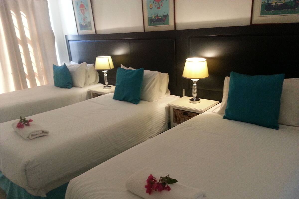 Quarto de hotel com duas camas de solteiro, cada uma com almofada e uma pequena mesa com abajur.