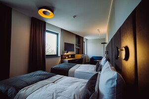 Quarto de hotel com duas camas, uma escrivaninha, uma cadeira, uma televisão e uma janela.