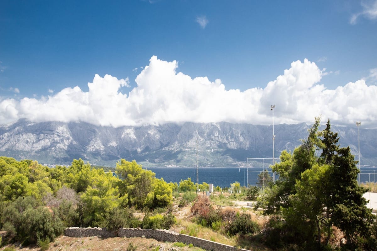 Paisagem montanhosa com céu claro, um corpo de água e vegetação densa.