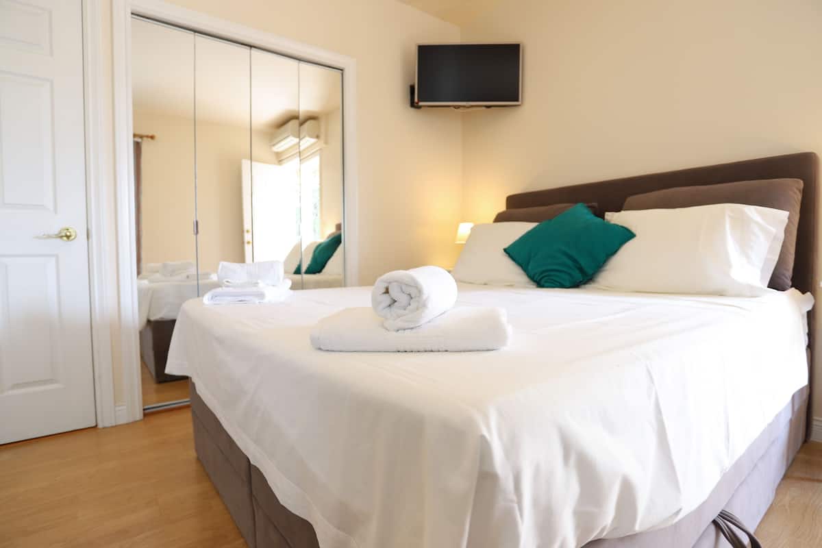 Cama bem arrumada com lençóis brancos, um travesseiro azul-esverdeado e uma toalha enrolada.