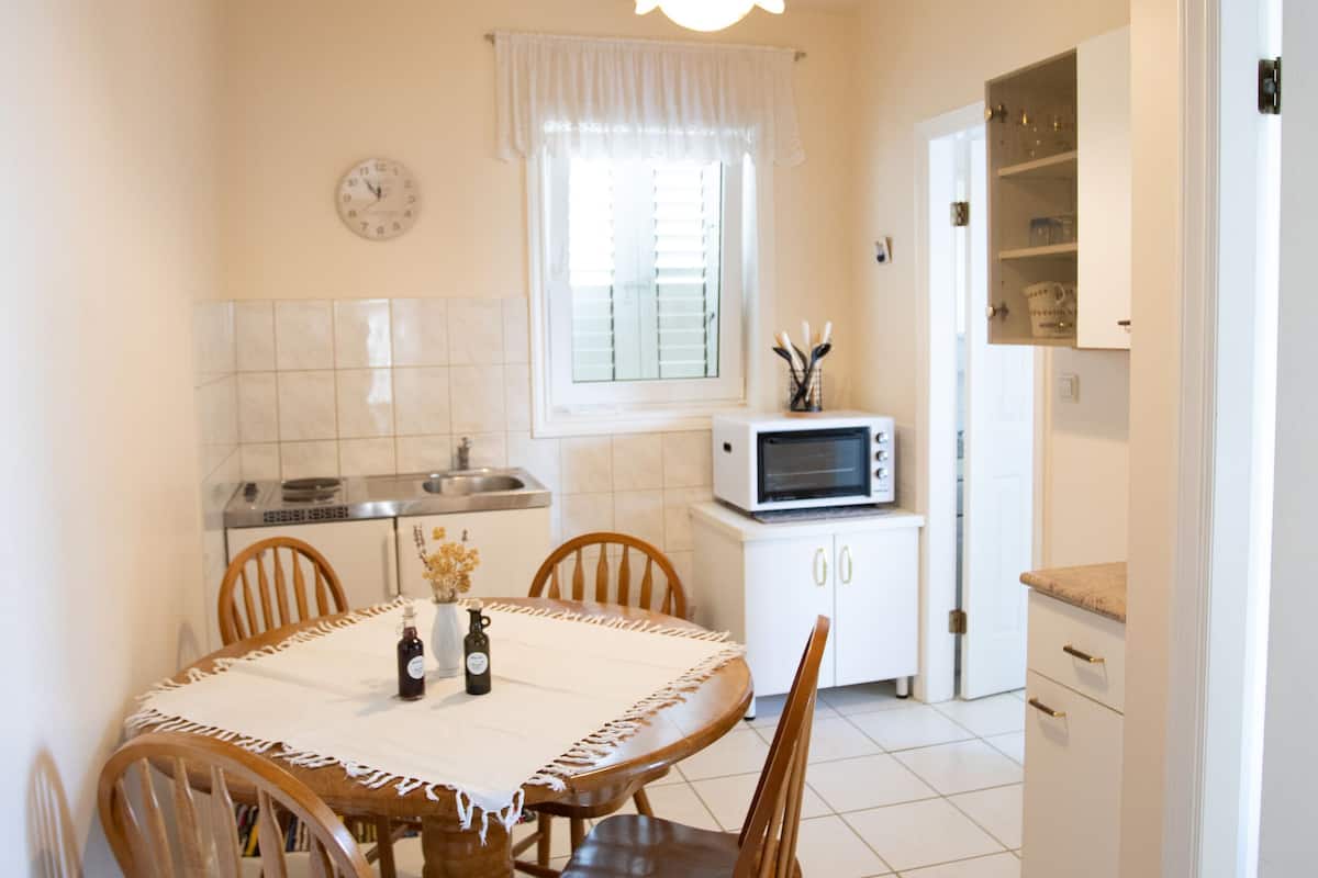 Uma cozinha pequena com uma mesa de jantar, cadeiras, micro-ondas e um relógio na parede.