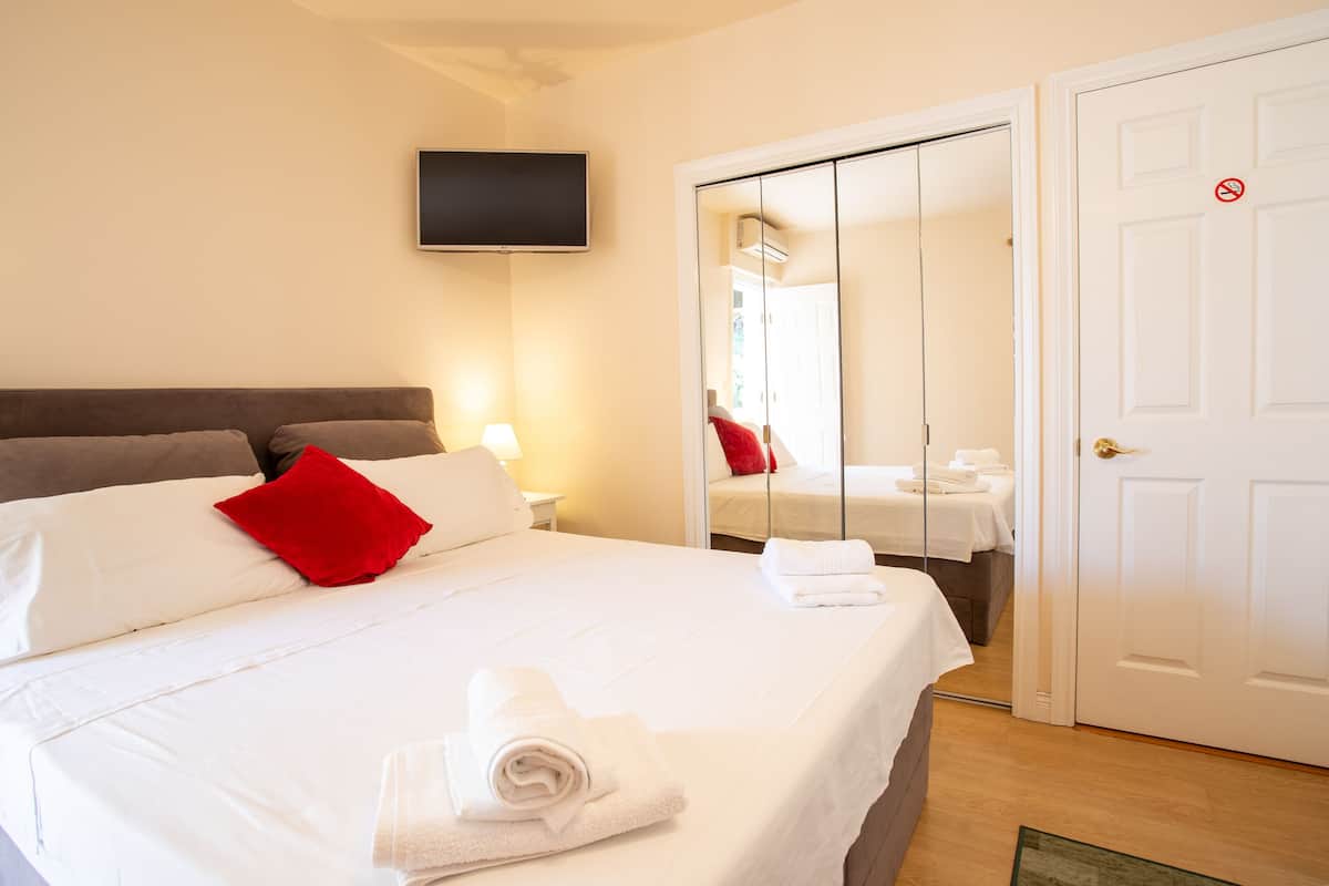 Quarto de hotel com cama, televisão fixada na parede, guarda-roupa e porta com placa de proibido fumar.
