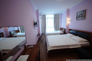 Quarto de hotel com duas camas, uma escrivaninha de madeira, um espelho, uma janela com cortinas e um quadro na parede.