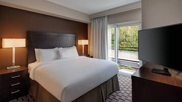 Quarto de hotel com uma cama grande, duas luminárias de cabeceira, uma televisão de tela plana e vista para o verde pela janela.