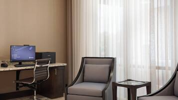 Quarto de hotel com escrivaninha, computador e duas poltronas.