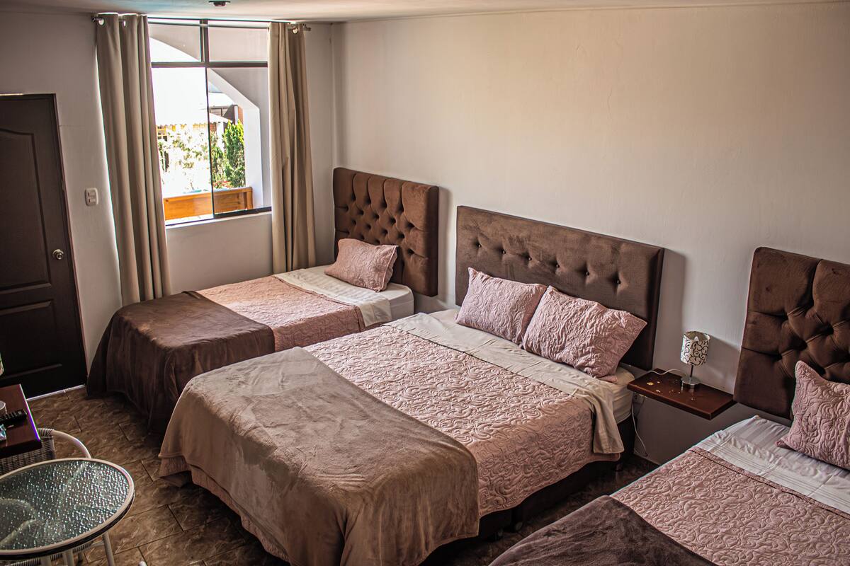 Quarto de hotel com duas camas, uma mesa pequena e janela com cortinas.
