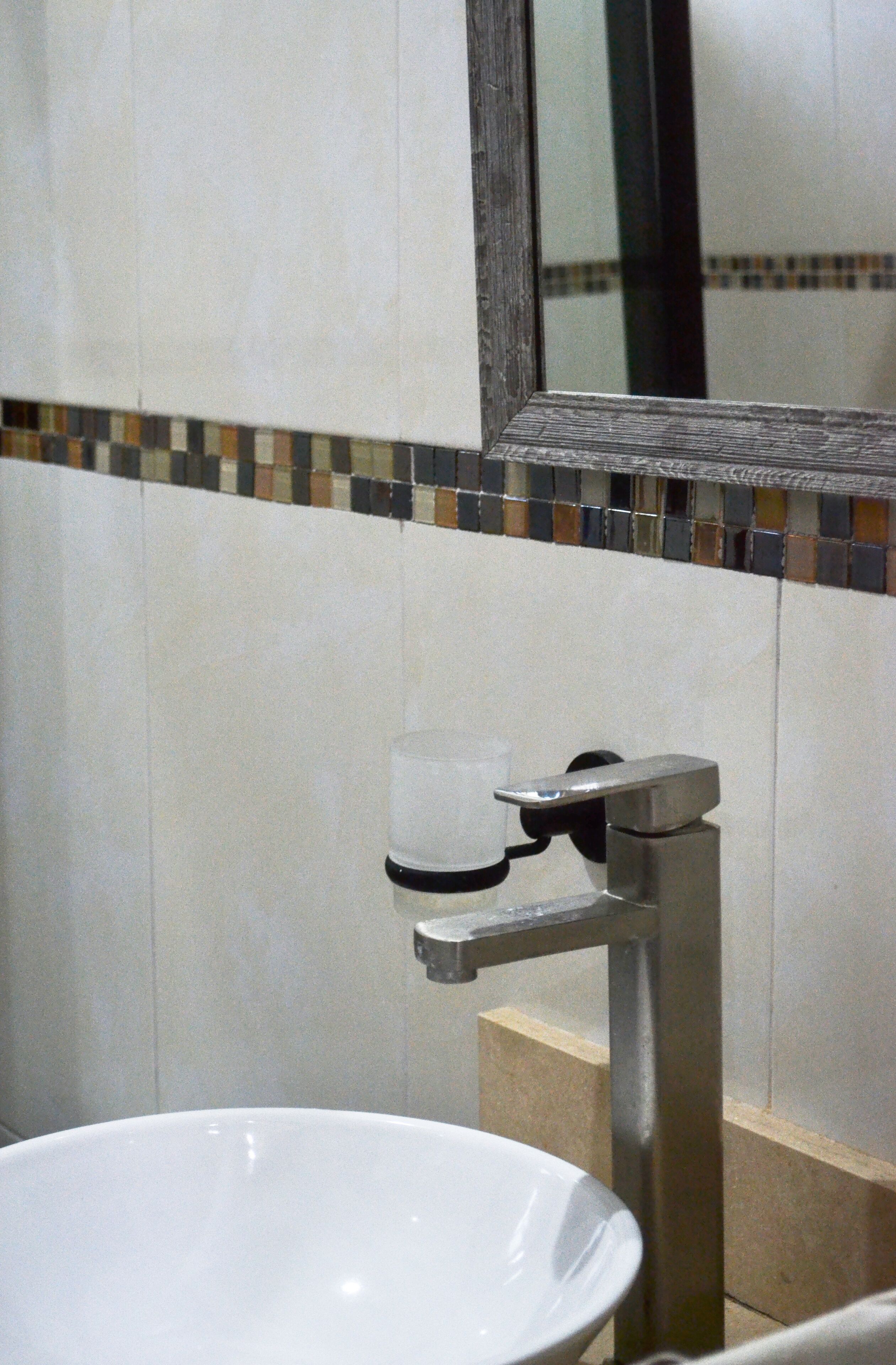 Casa de banho com lavatório branco, espelho e painel de azulejos.