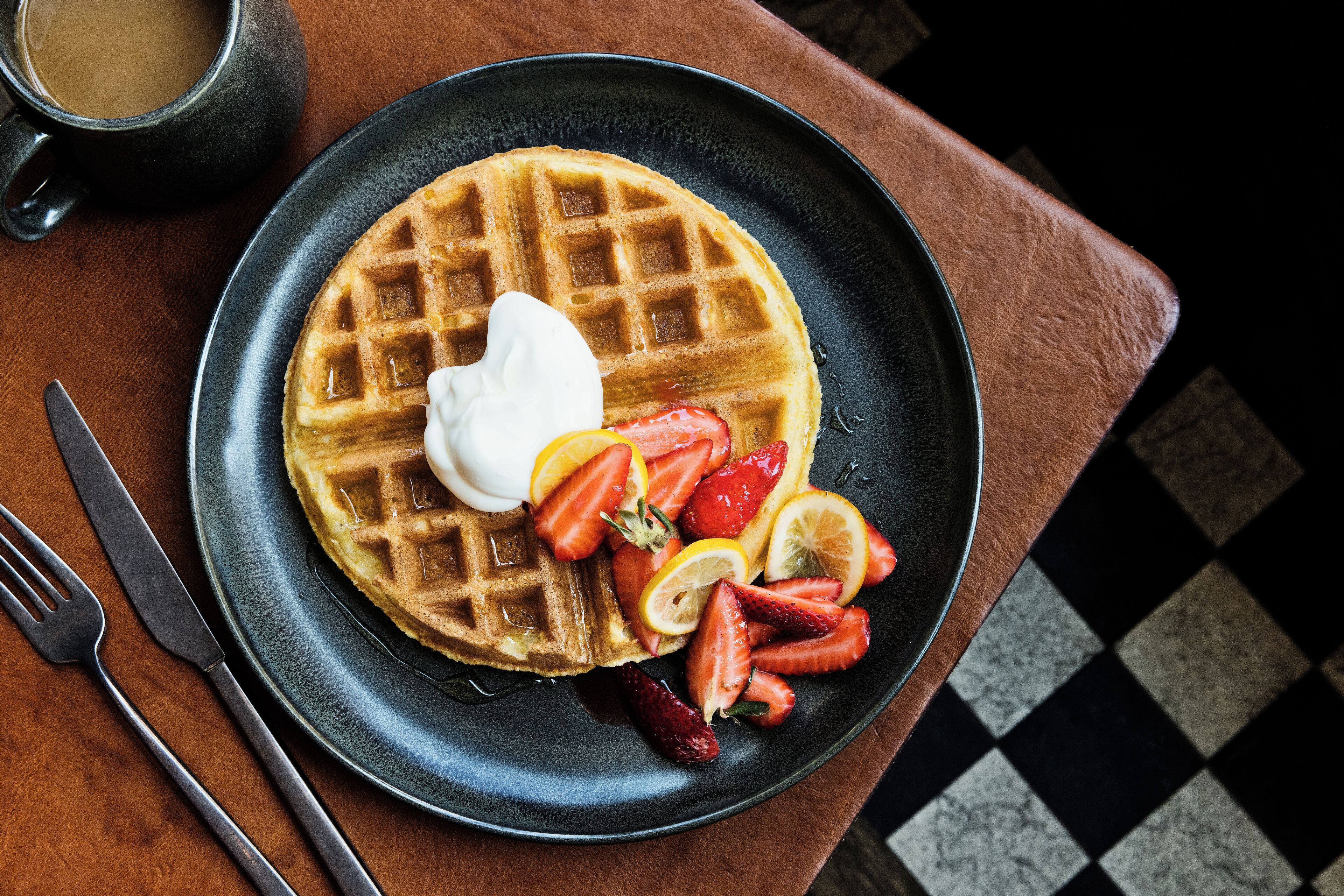 Um prato com um waffle, morangos e rodelas de limão sobre um prato escuro.