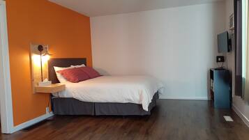 Quarto com cama, mesa de cabeceira com abajur e TV na parede.