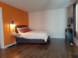 Quarto com cama, mesa de cabeceira com abajur e TV na parede.
