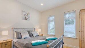Um quarto bem arrumado com uma cama de estrutura metálica, duas mesas de cabeceira com luminárias e duas janelas com persianas.