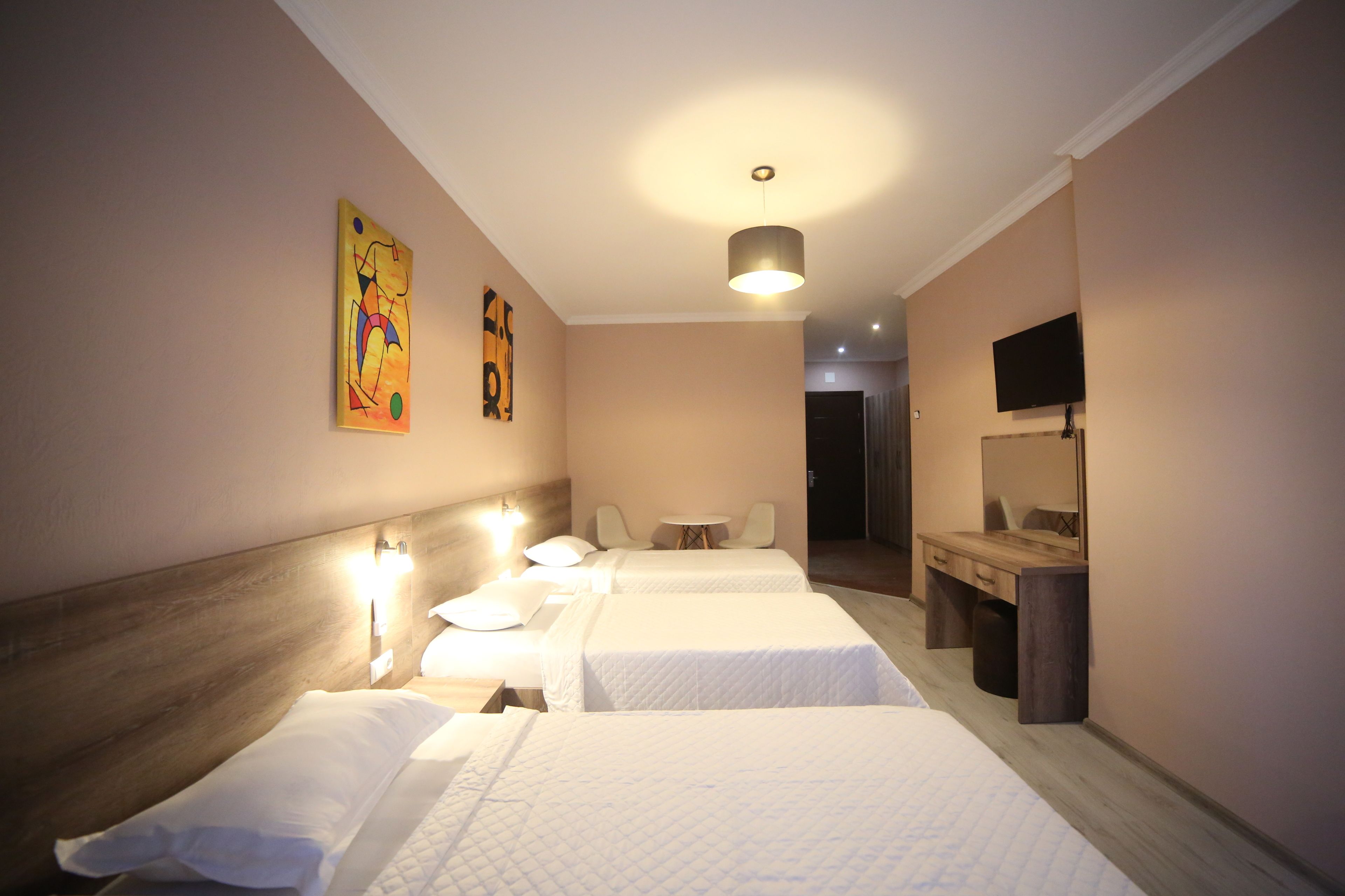 Quarto de hotel com duas camas, uma mesa, uma cadeira, televisão e obras de arte na parede.