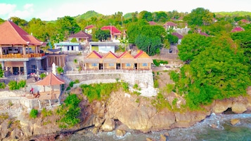 Um resort costeiro com vários edifícios, alguns com telhados vermelhos, situado em um penhasco com vista para um rio.