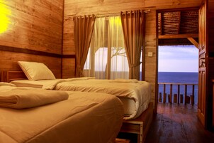 Quarto de cabana de madeira com duas camas, uma varanda com guarda-corpo e vista para o oceano.