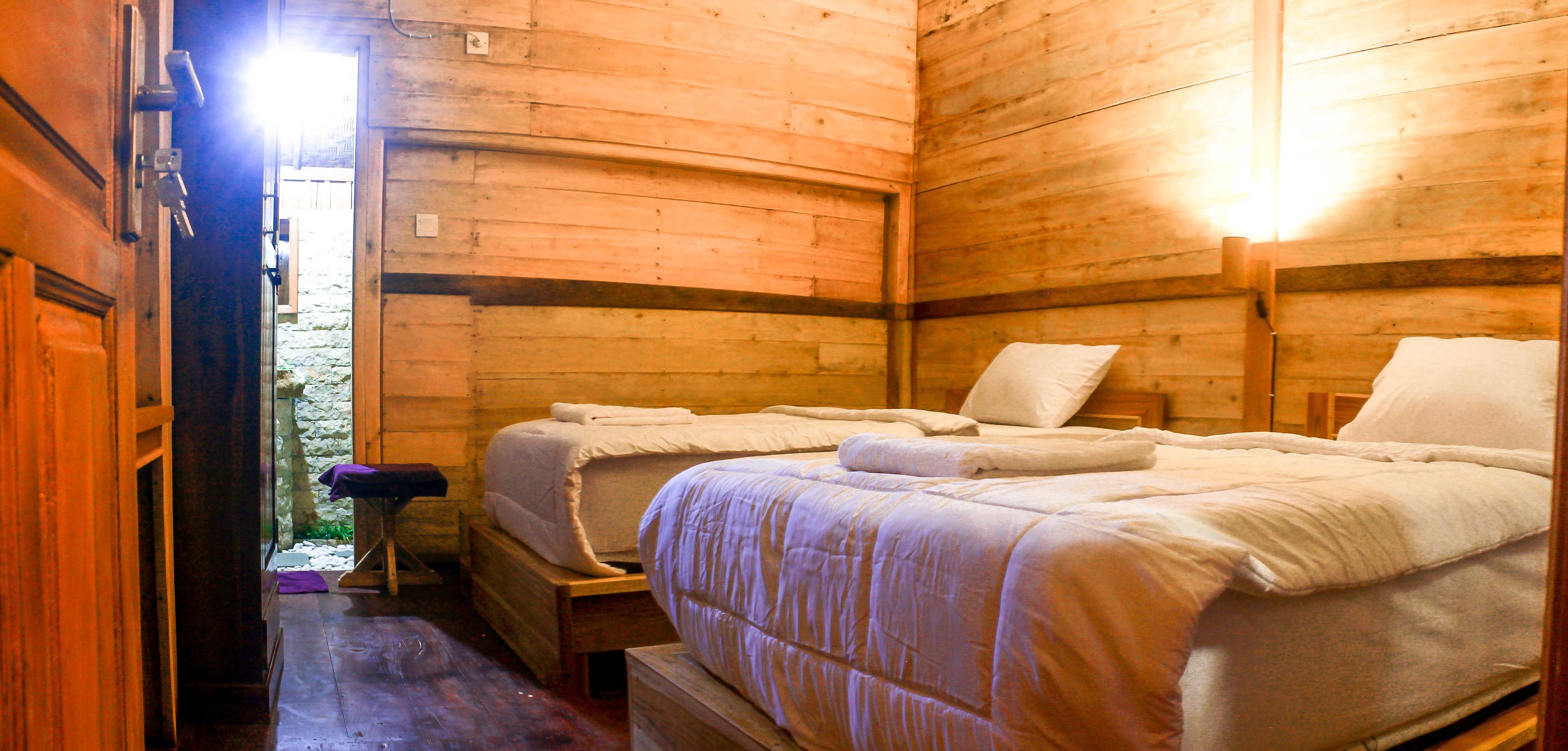 Quarto de cabana de madeira com duas camas, um banco e uma janela pequena.