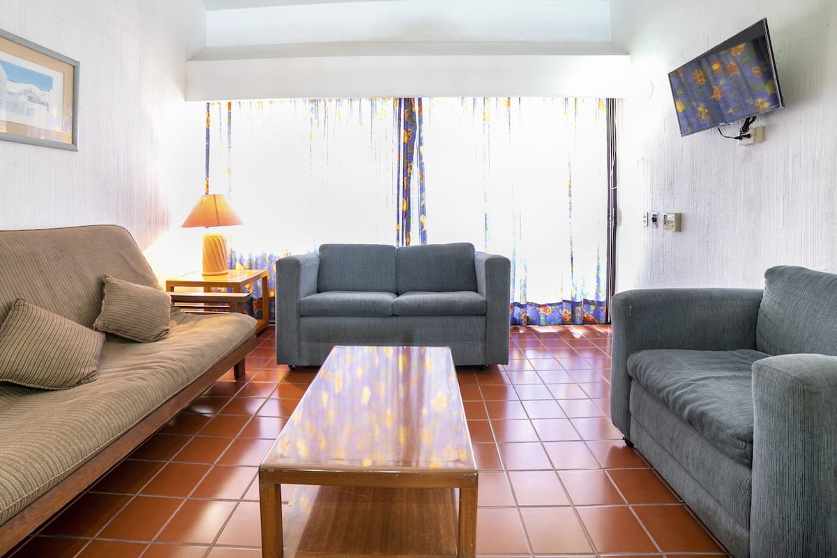 Uma sala de estar com sofá, mesa de centro e televisão na parede.
