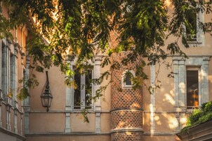 Fachada de edifício com torre de tijolos, janelas com persianas e um lança-luz pendurado.