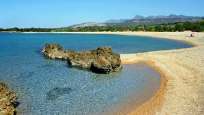 Uma praia com águas cristalinas, formações rochosas e montanhas ao longe.