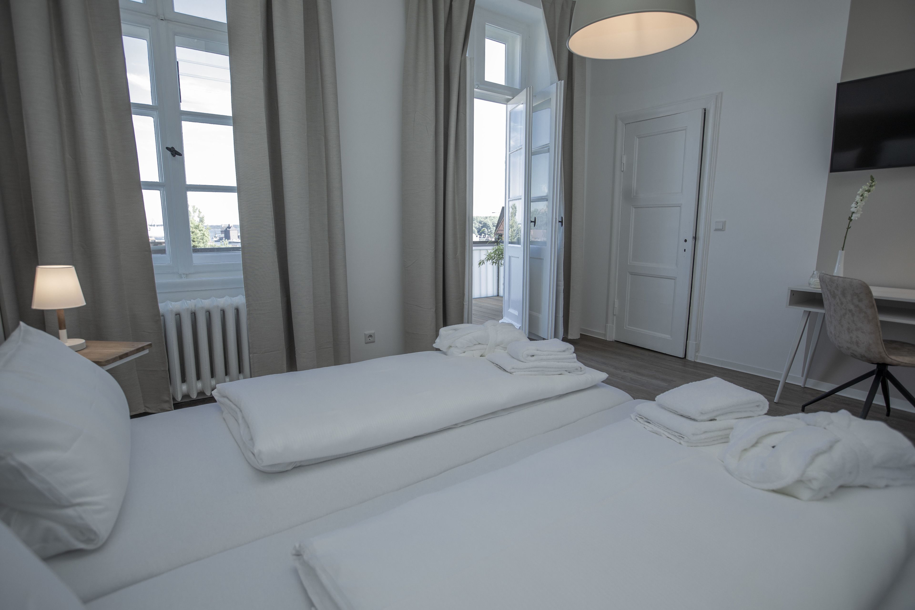 Quarto de hotel com duas camas, uma escrivaninha, uma cadeira, televisão e vista para o exterior.