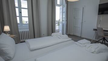 Quarto de hotel com duas camas, uma escrivaninha, uma cadeira, televisão e vista para o exterior.