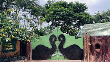 Um portão com design exclusivo, uma placa indicando Coorg Jungle Camp e vegetação exuberante ao fundo.