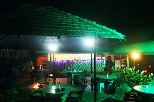 Uma área externa com mesas e cadeiras, piso de azulejos e uma parede iluminada em verde.