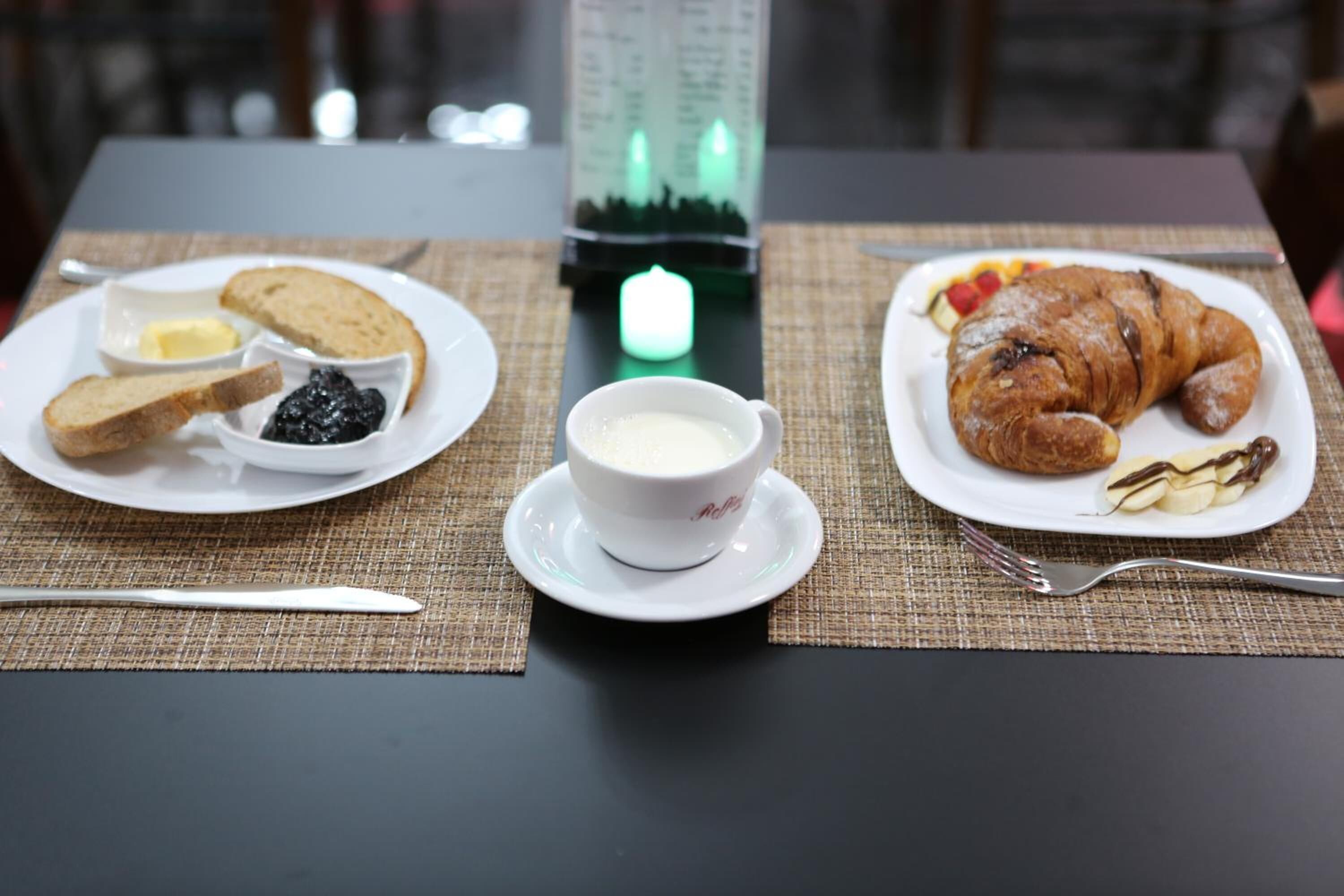 Uma mesa com dois pratos de comida, uma xícara de café e uma vela.